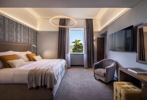 Quarto de hotel moderno com uma cama grande, área de estar e televisão.