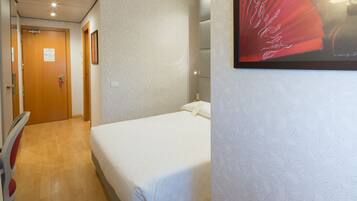 Quarto de hotel com piso de madeira, cama com roupa de cama branca, porta com uma placa e um quadro na parede.