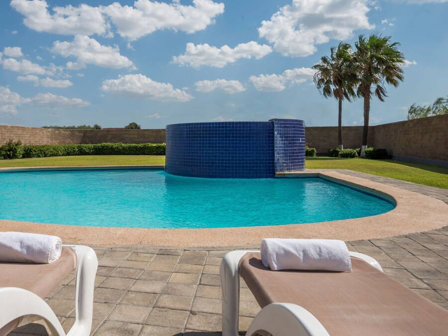 Piscina com duas espreguiçadeiras e uma banheira de hidromassagem azulejada em azul.