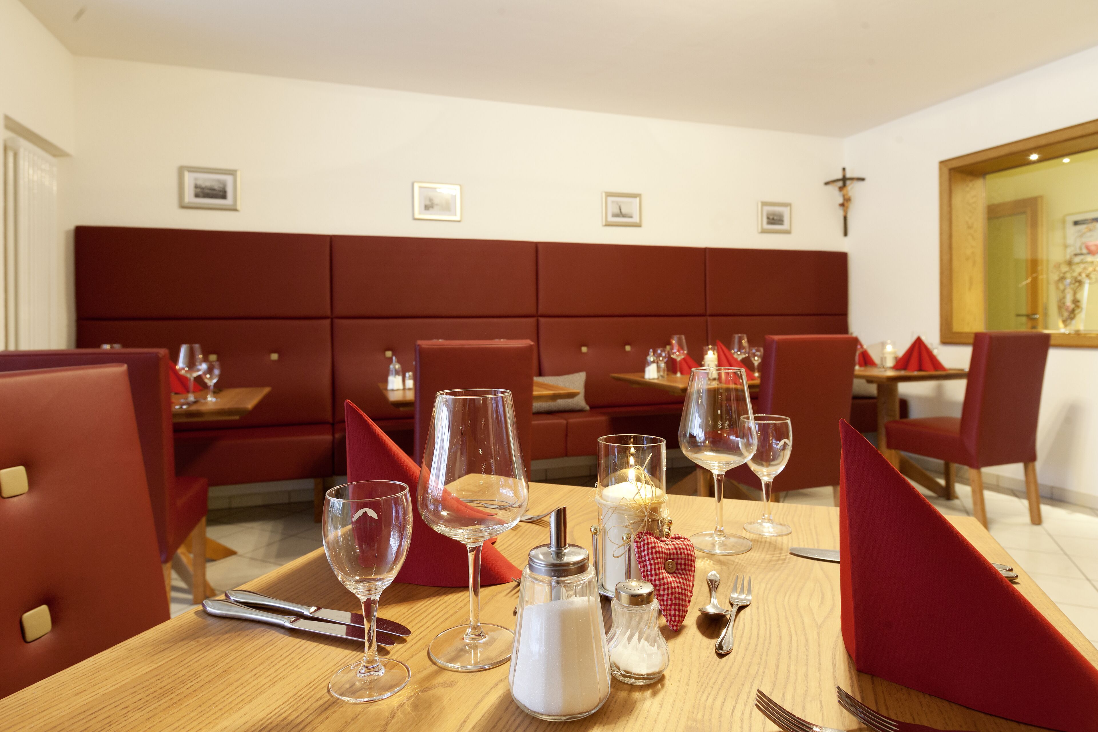 Uma sala de jantar com mesas de madeira, cadeiras estofadas em vermelho e uma cruz na parede.