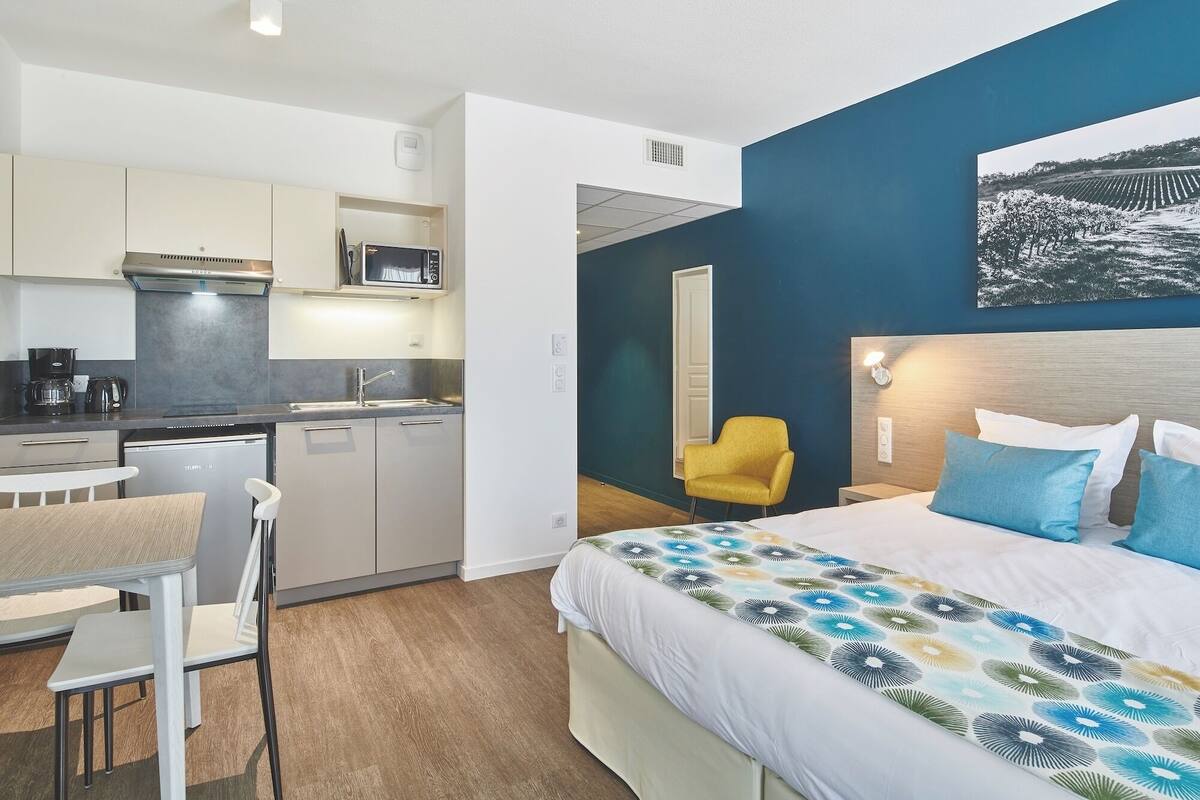 Quarto de hotel compacto com cama, pequeno espaço de cozinha, área de refeições e banheiro.