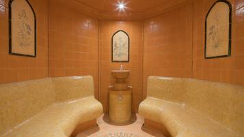 Um espaço de spa com duas áreas de assento acolchoadas, uma fonte central e azulejos decorativos nas paredes.