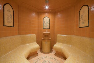 Um espaço de spa com duas áreas de assento acolchoadas, uma fonte central e azulejos decorativos nas paredes.