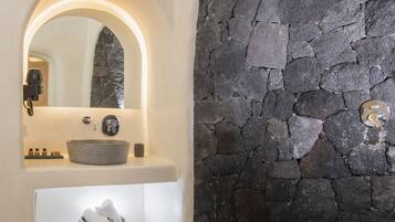 Uma casa de banho com parede de pedra, lavatório redondo e espelho com arco.