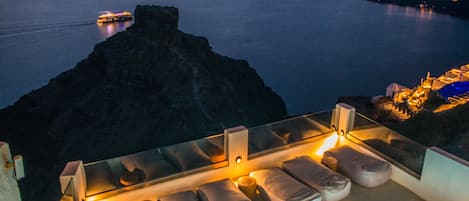 Terraço no telhado com vista para o mar, guarda-corpo de vidro e área de piscina com espreguiçadeiras.