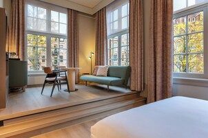 Quarto de hotel com cama, sofá verde, cadeira, mesa pequena e radiador.