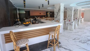 Uma cozinha moderna com ilha central, banquetas e área de refeições com cadeiras e mesas brancas.
