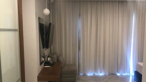 Uma sala de estar ampla com sofá, mesa de centro de madeira e uma grande janela com cortinas.