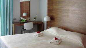 Quarto de hotel com cama, escrivaninha, cadeira, luminária e uma cesta de frutas.