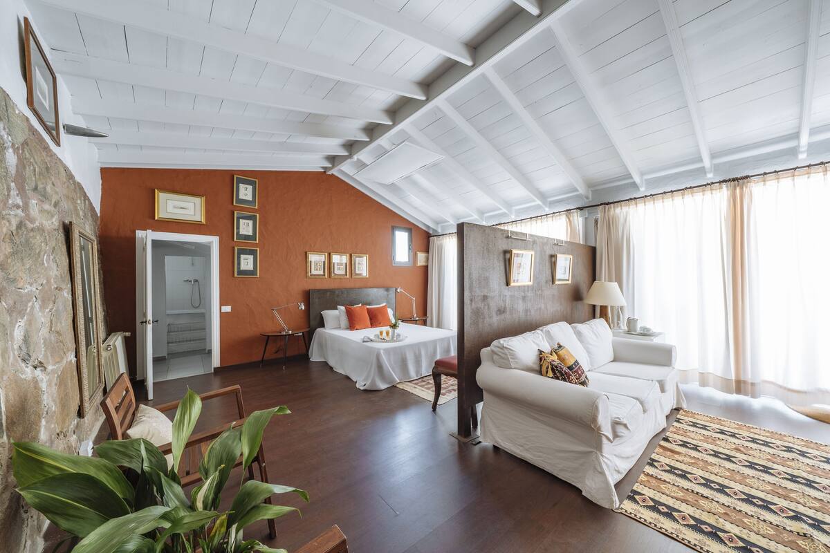 Uma sala de estar espaçosa com teto alto, uma cama, um sofá e um espaço para refeições.