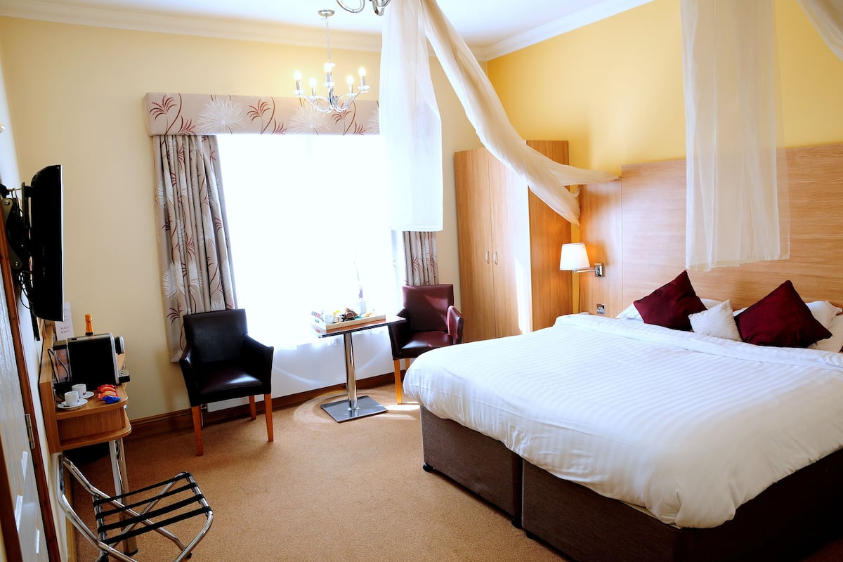 Quarto de hotel com uma cama grande, uma escrivaninha com cadeira, televisão e janela com cortinas.