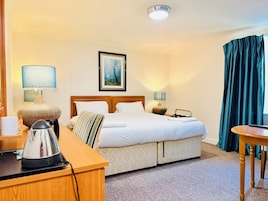 Quarto de hotel com cama, abajures, um quadro, escrivaninha com chaleira e vista para o exterior.
