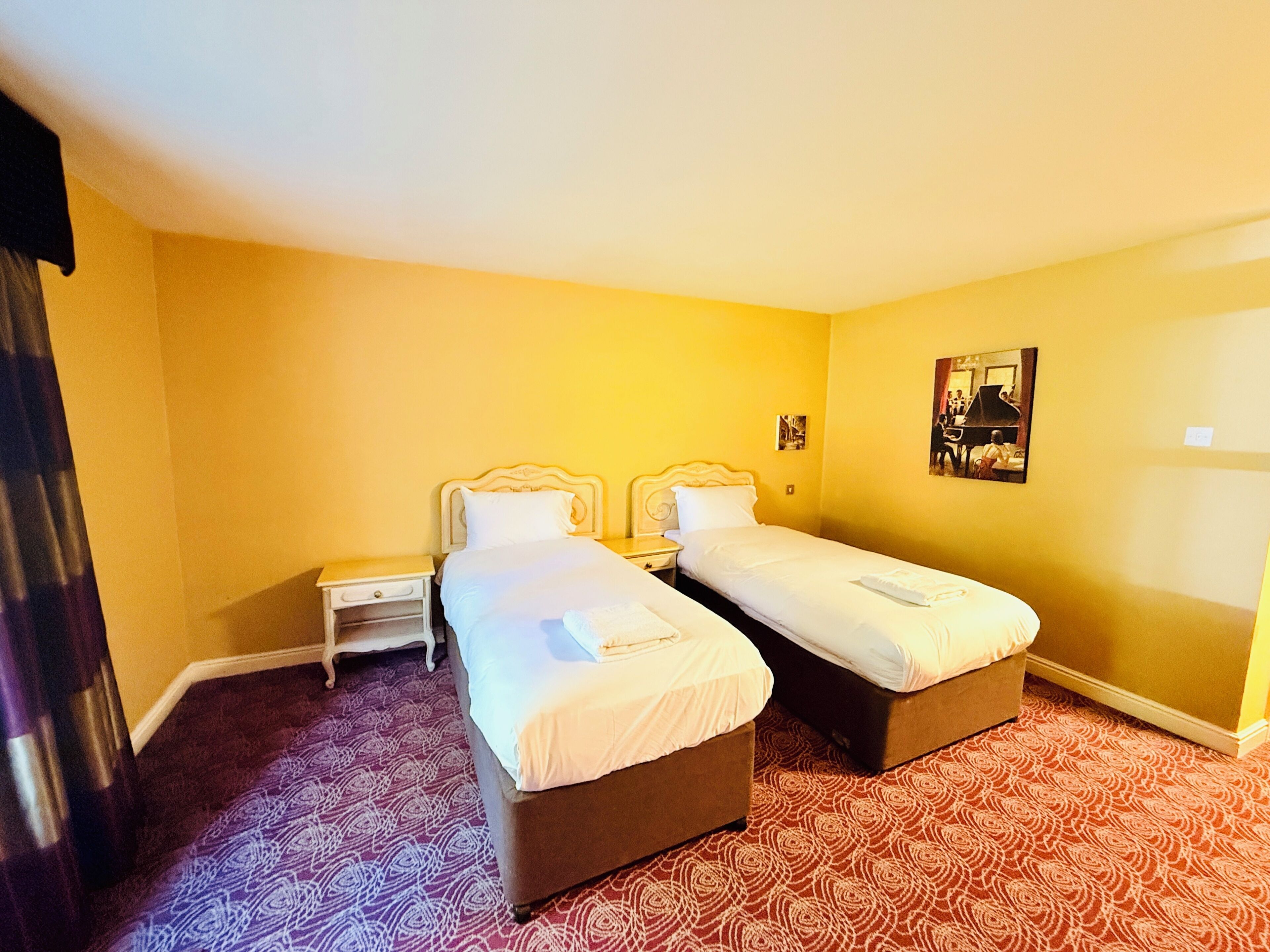 Quarto de hotel com duas camas, uma mesinha de cabeceira e um tapete estampado.