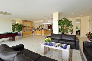 Um saguão de hotel com mesa de bilhar, sofás de couro, balcão de recepção e plantas em vasos.