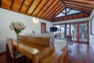 Uma mesa de jantar de madeira com cadeiras, um vaso de flores e uma cama com vista para o exterior.