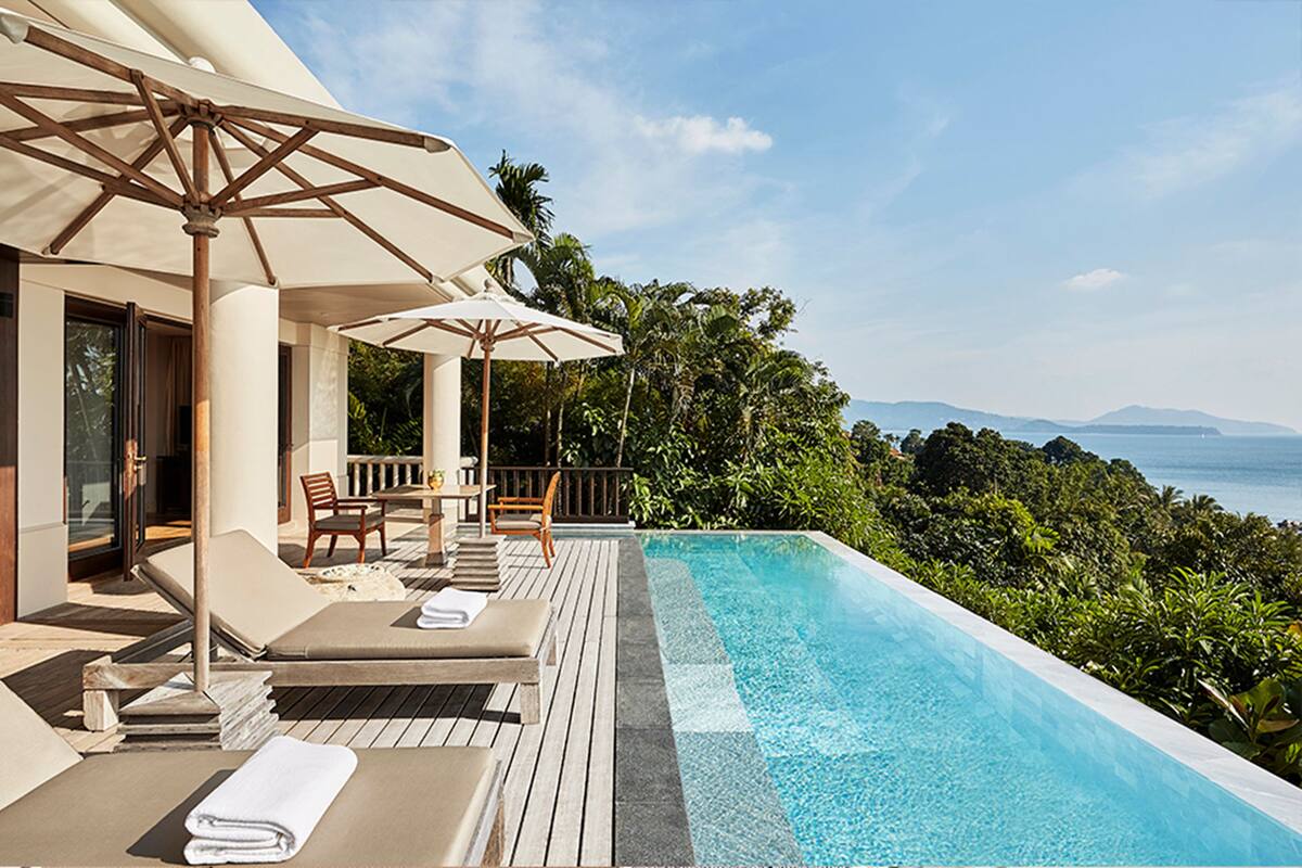 Uma área à beira da piscina com espreguiçadeiras, guarda-sóis e vista para o oceano.