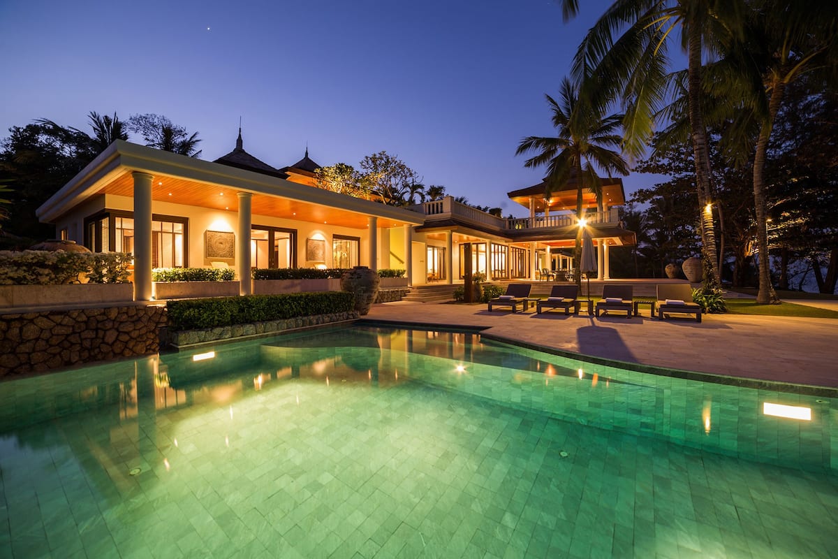 Um resort luxuoso com piscina, área de estar externa e um edifício bem iluminado ao entardecer.