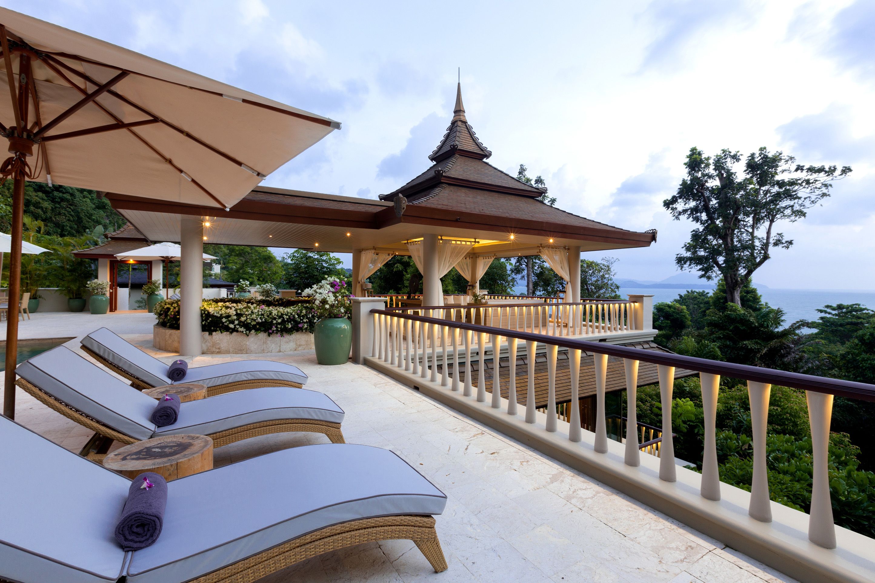Um terraço com cadeiras de descanso, um gazebo e vista para o mar.