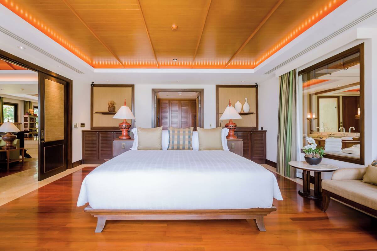 Um quarto de hotel espaçoso com uma cama grande, piso de madeira e design moderno no teto.