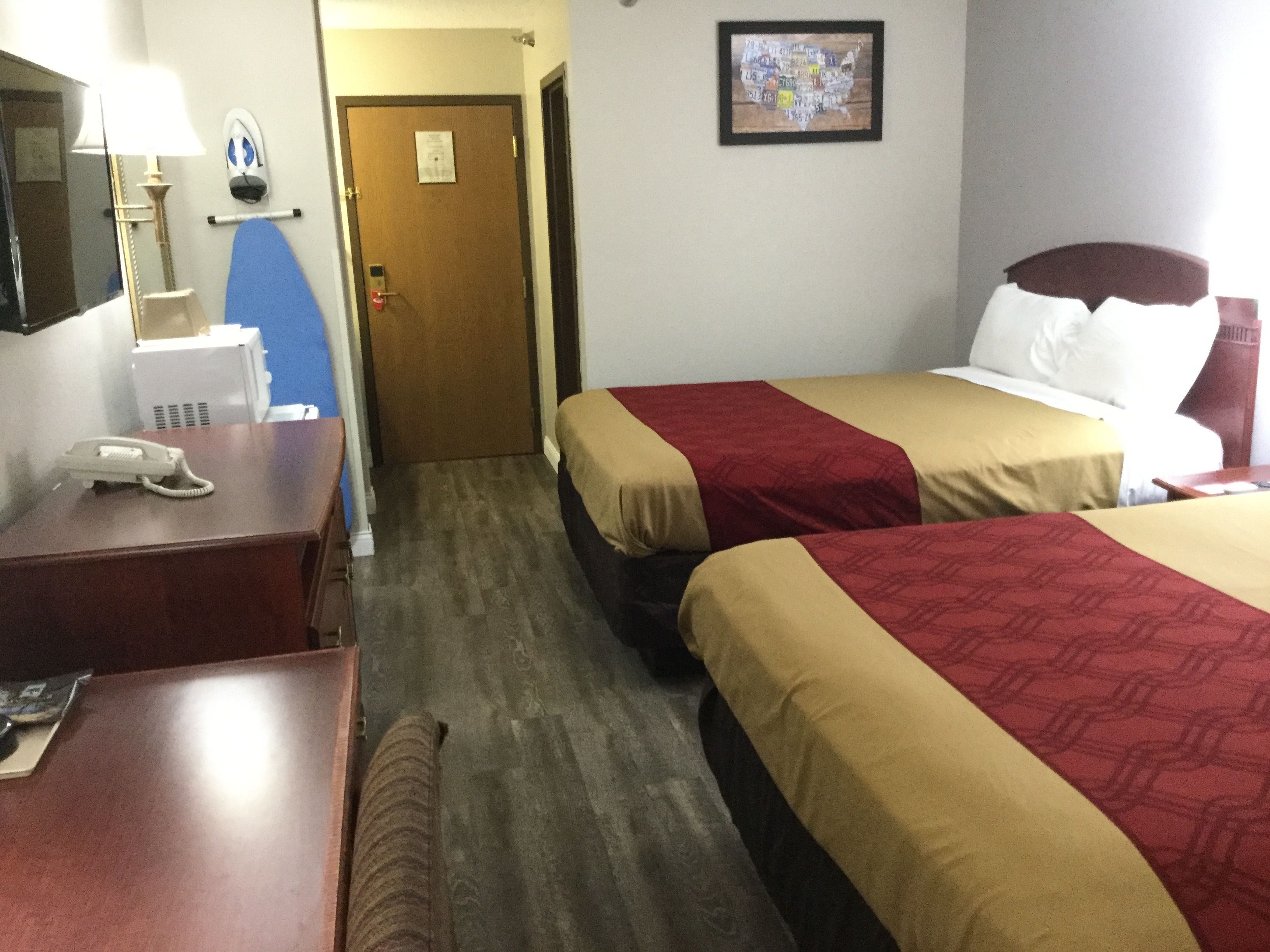 Quarto de hotel com duas camas, uma escrivaninha com telefone, uma luminária e um mapa emoldurado na parede.