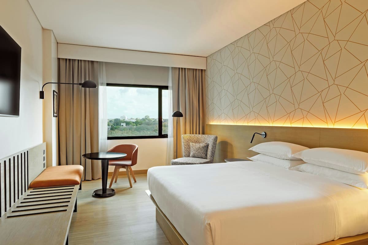 Quarto de hotel com cama, escrivaninha, cadeira e janela com cortinas.