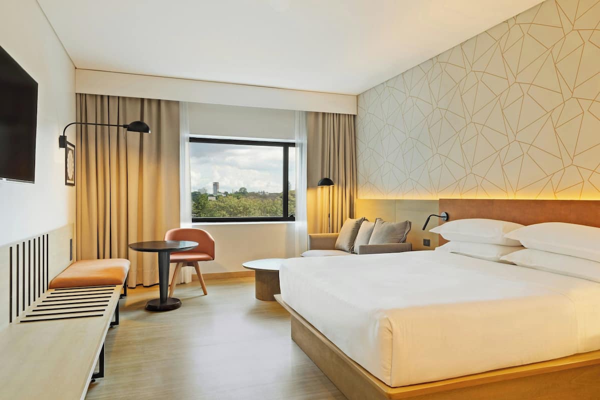 Quarto de hotel com uma cama grande, uma escrivaninha, uma cadeira e vista para a cidade.