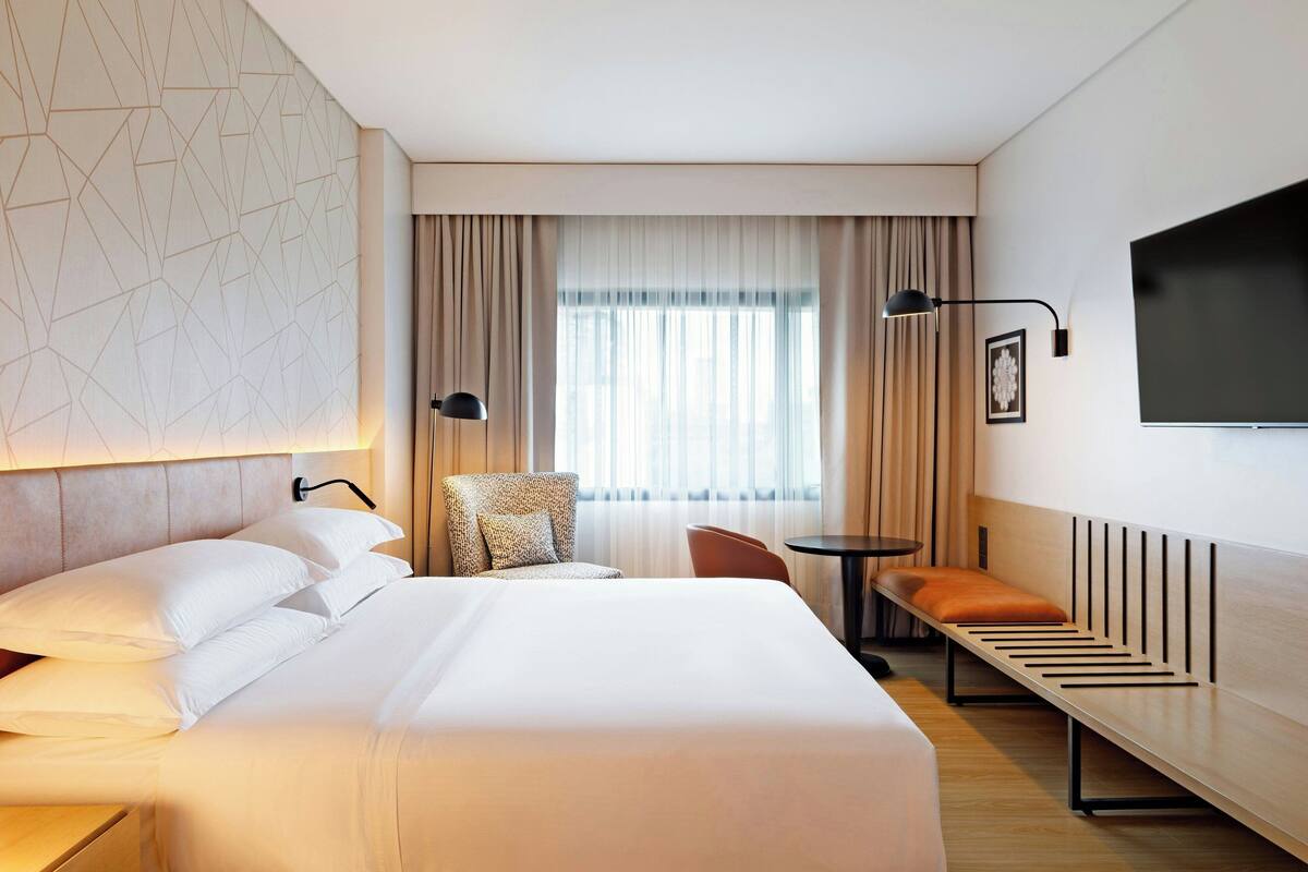 Quarto de hotel moderno com uma cama grande, uma escrivaninha, uma cadeira e uma televisão.