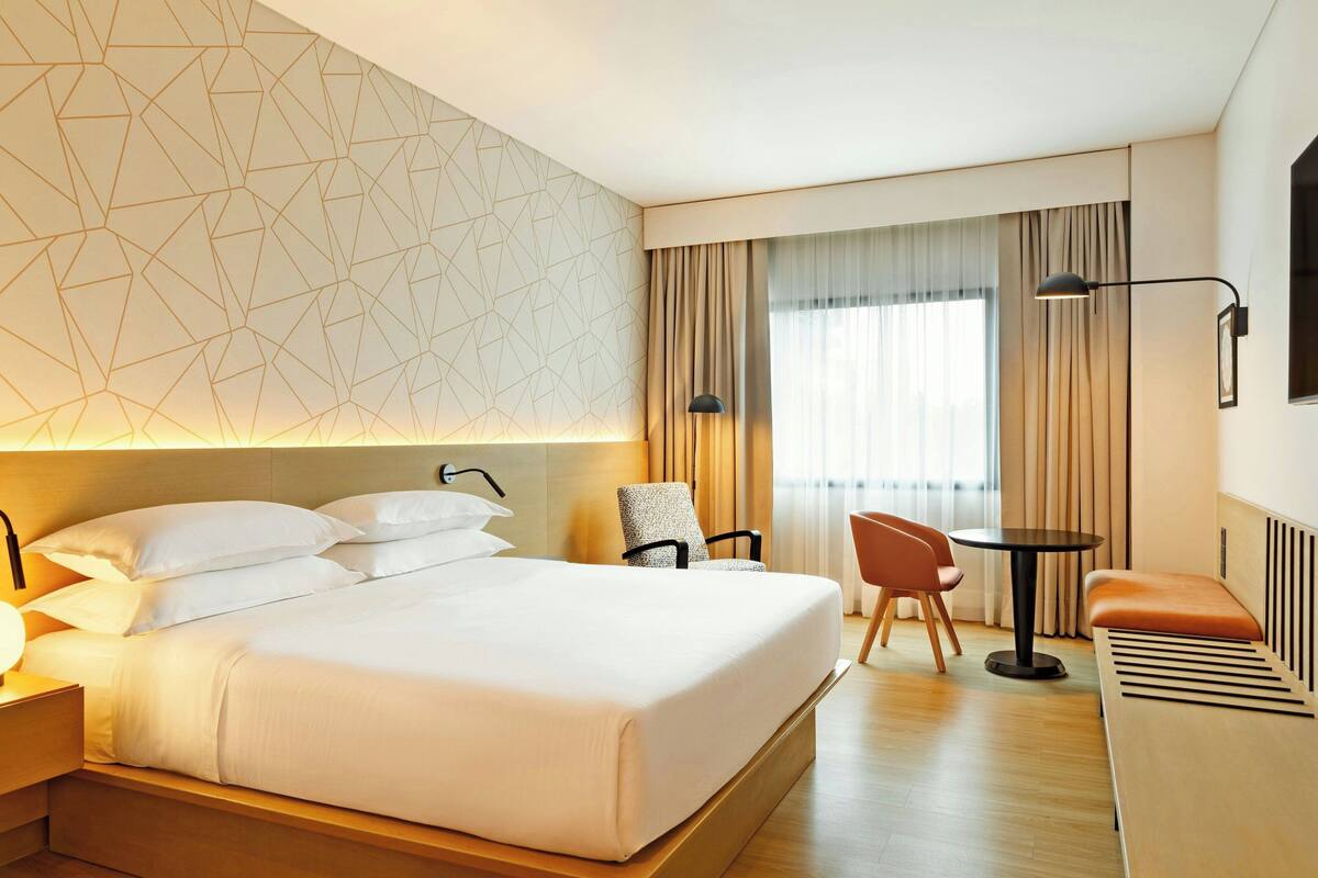 Quarto de hotel moderno com uma cama grande, uma escrivaninha, uma cadeira e um sofá.
