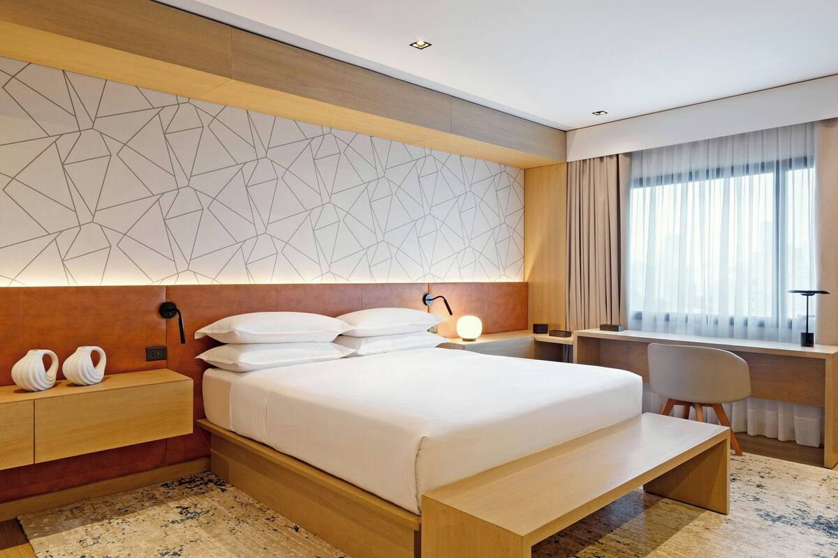 Quarto de hotel moderno com uma cama grande, mesas de cabeceira, uma escrivaninha e uma cadeira.