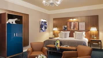 Quarto de hotel com uma cama grande, duas luminárias laterais, uma cabeceira de madeira, um guarda-roupa com uma figura de urso polar e um candelabro.