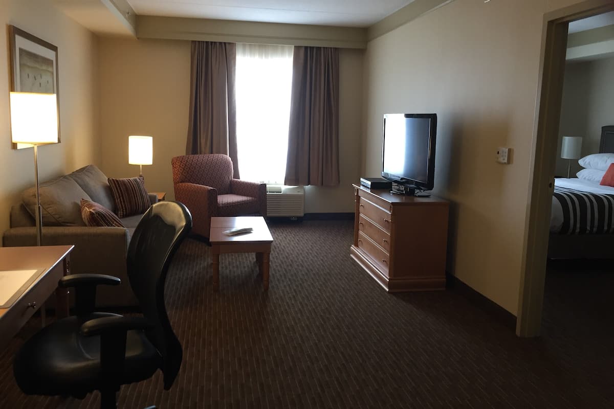Quarto de hotel com sofá, poltrona, escrivaninha, cadeira, cômoda, televisão e cama.