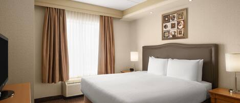 Quarto de hotel com cama grande, televisão de tela plana, escrivaninha e janela com cortinas.