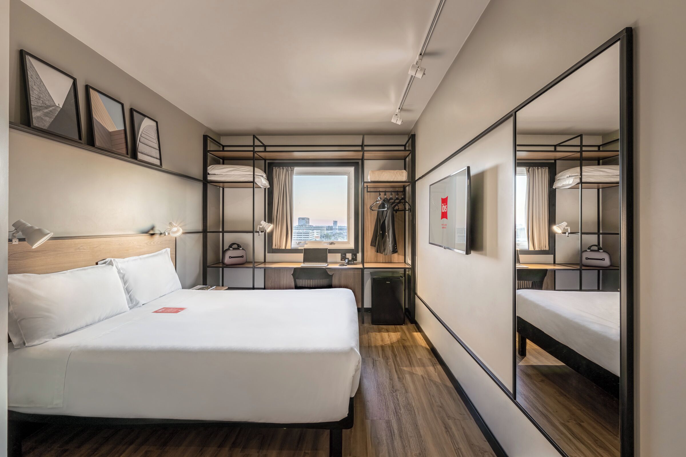 Quarto de hotel com cama, escrivaninha, cadeira e espelho.