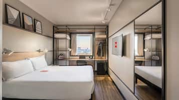 Quarto de hotel com cama, escrivaninha, cadeira e espelho.