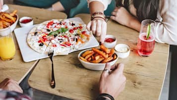 Uma mesa de jantar com pizza, batatas fritas e bebidas.