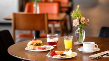 Uma mesa de café da manhã posta para duas pessoas, com pratos de comida, um copo de suco de laranja e uma xícara de café.