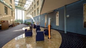 Um hall amplo com pé-direito alto, área de estar central e uma grande janela que traz luz natural.