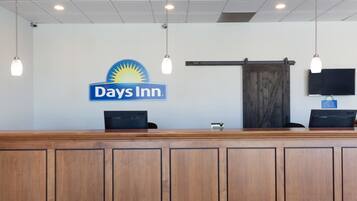 Bancada de recepção com a placa Days Inn, balcão de madeira, dois monitores de computador e uma televisão montada.