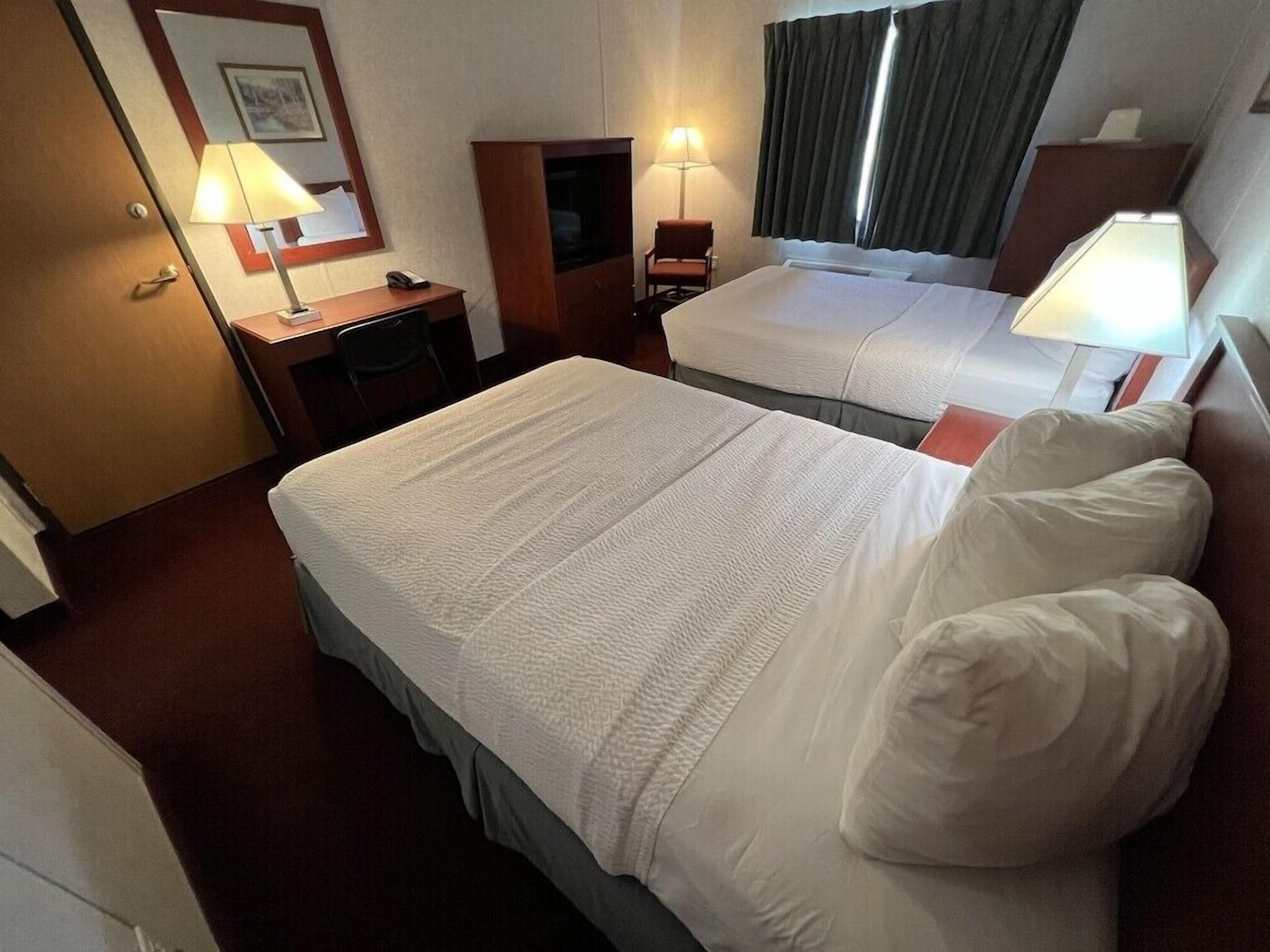 Quarto de hotel com duas camas, uma escrivaninha, uma cadeira e duas luminárias.