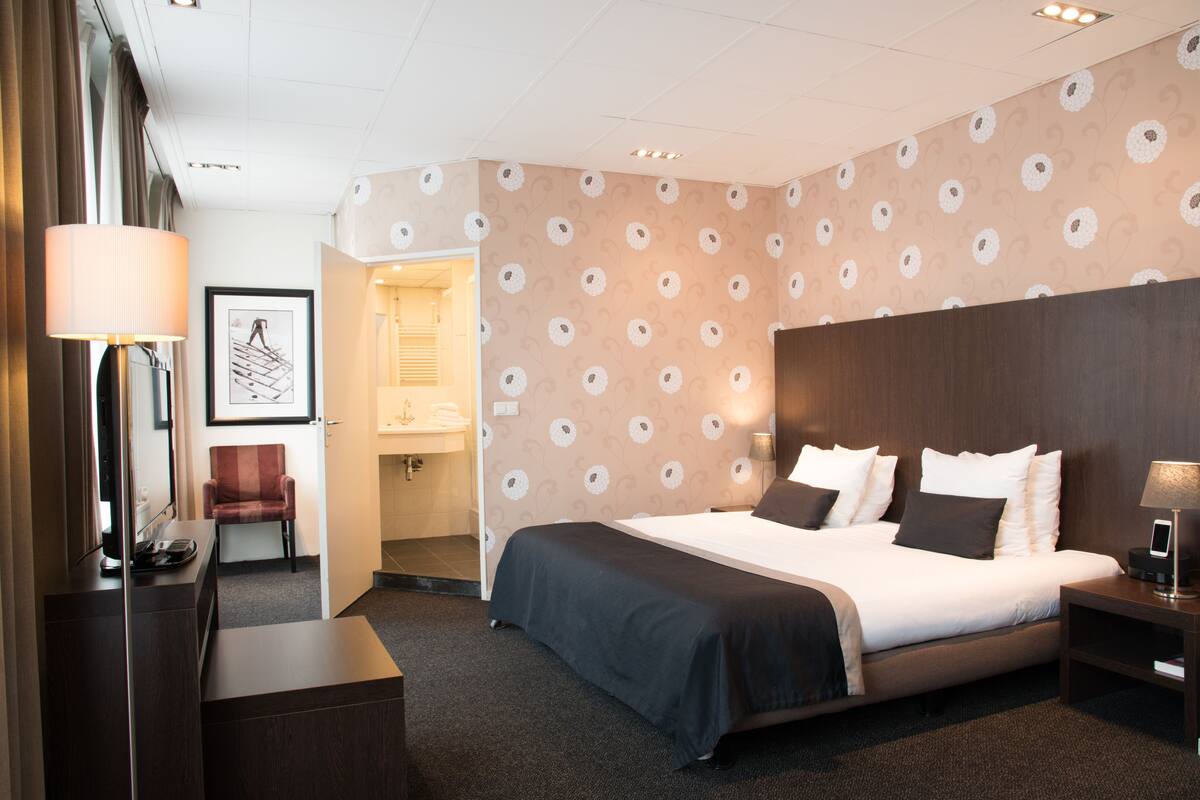 Quarto de hotel com uma cama grande, uma escrivaninha, uma cadeira e um banheiro visível por uma porta aberta.