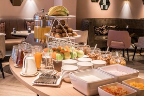 Buffet de café da manhã com diversas frutas, bebidas e opções para o pequeno-almoço.