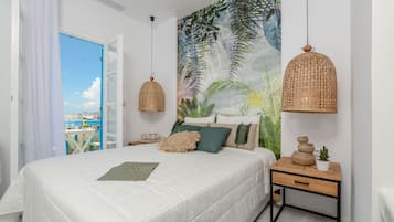 Quarto com uma cama grande, uma mesa de cabeceira, uma luminária de rattan pendente e vista do céu através de uma porta aberta.