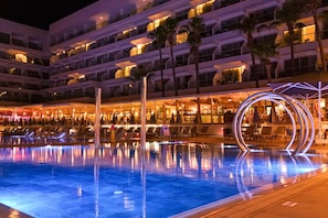 Uma área de piscina de hotel com vários níveis de varandas, espreguiçadeiras e um recurso de iluminação decorativa.