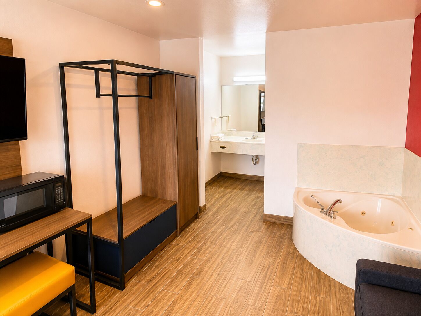 Casa de banho moderna com soalho de madeira, cabine de duche com estrutura preta, lavatório branco, banheira e um banco amarelo.