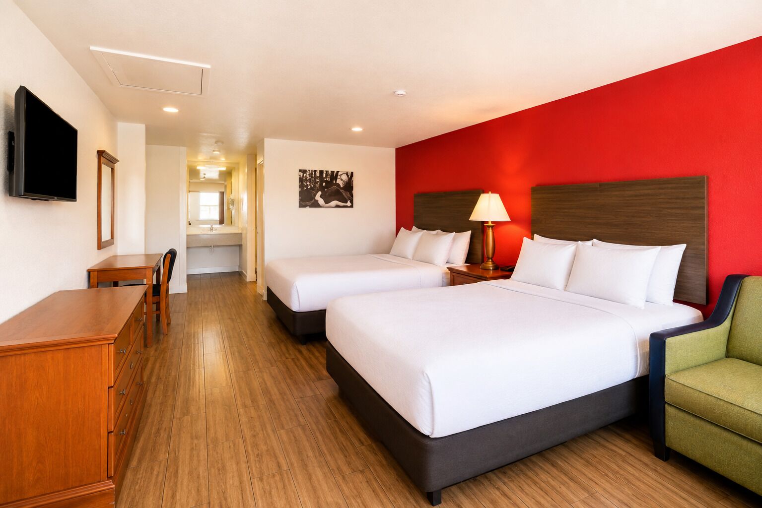 Quarto de hotel com duas camas, uma escrivaninha, uma cadeira, uma televisão e uma parede com detalhes vermelhos.