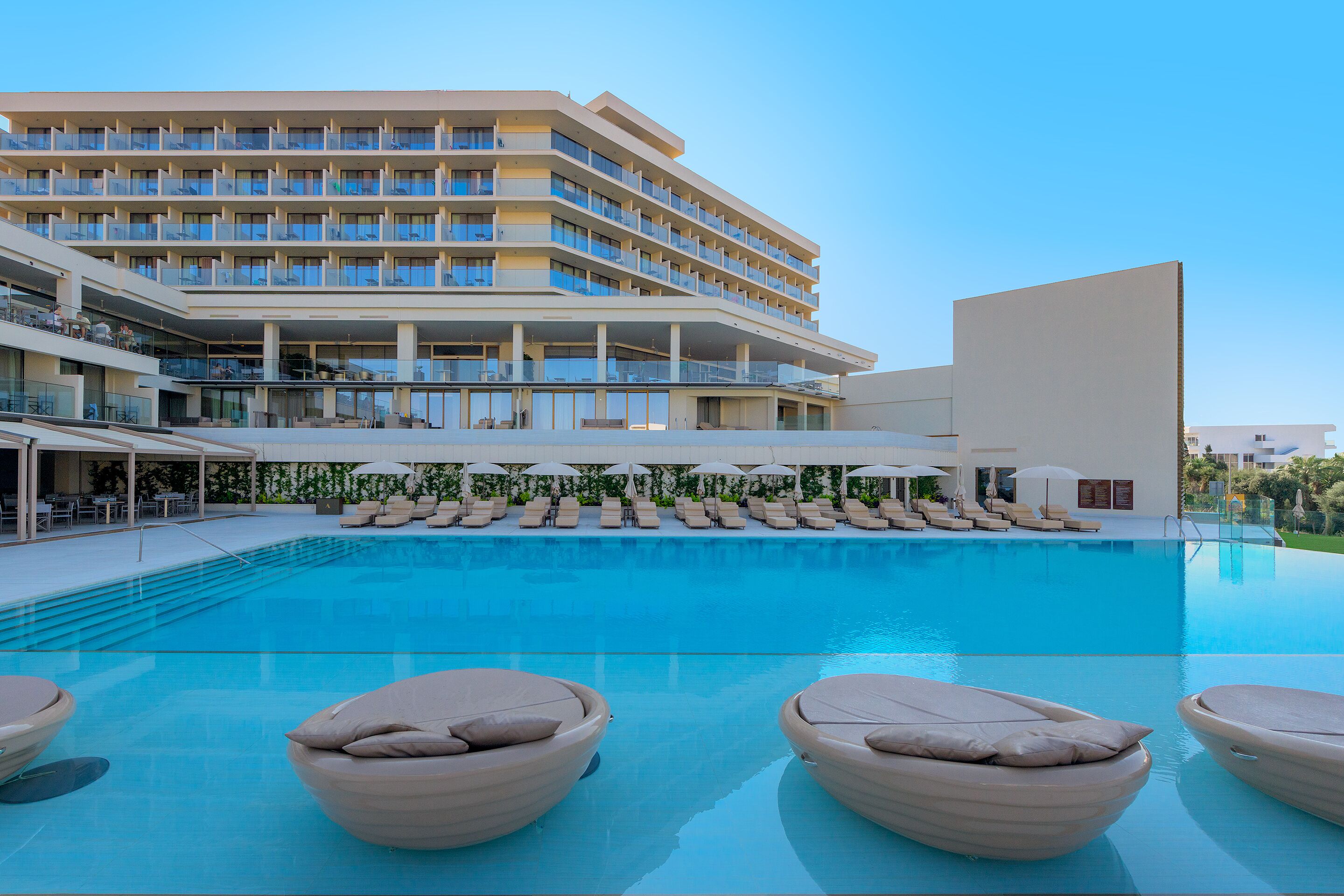 Um hotel com piscina grande, várias varandas e áreas de estar ao ar livre.