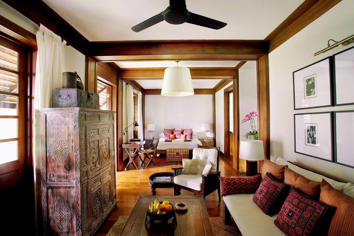 Quarto de hotel com teto de madeira, uma cama, um sofá, uma mesa de centro com frutas e um armário.