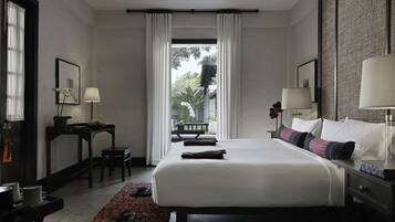 Quarto de hotel com uma cama grande, uma escrivaninha com luminária, vista para o exterior e uma janela ampla com cortinas.