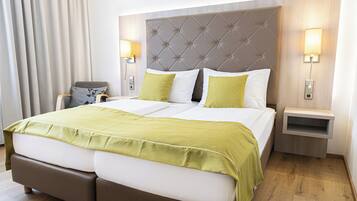 Uma cama de casal com cabeceira estofada, duas mesas de cabeceira com luminárias, um banquinho no pé da cama e piso de madeira.