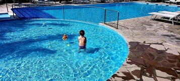 Piscina com uma criança e um brinquedo na água, rodeada por espreguiçadeiras e um deck de pedra.